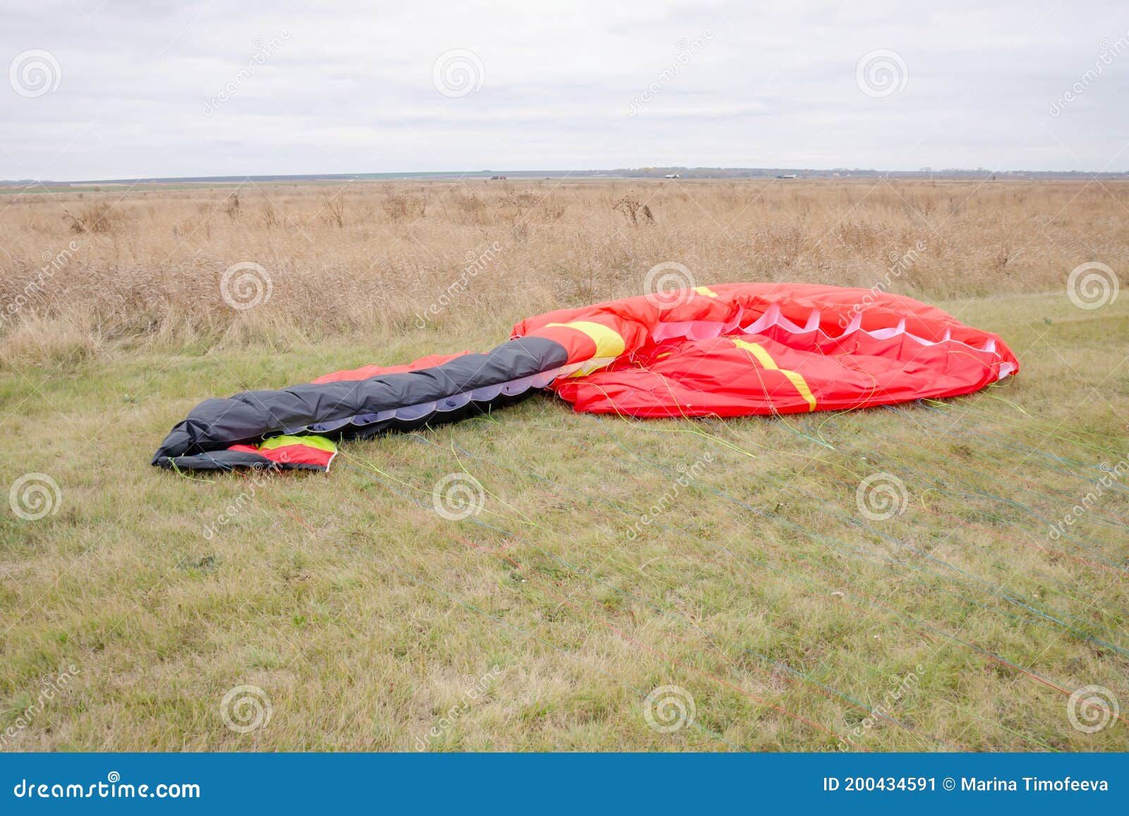 Red and Black Canopy Paraglider Lying on Green Grass Against a Cloudy ...