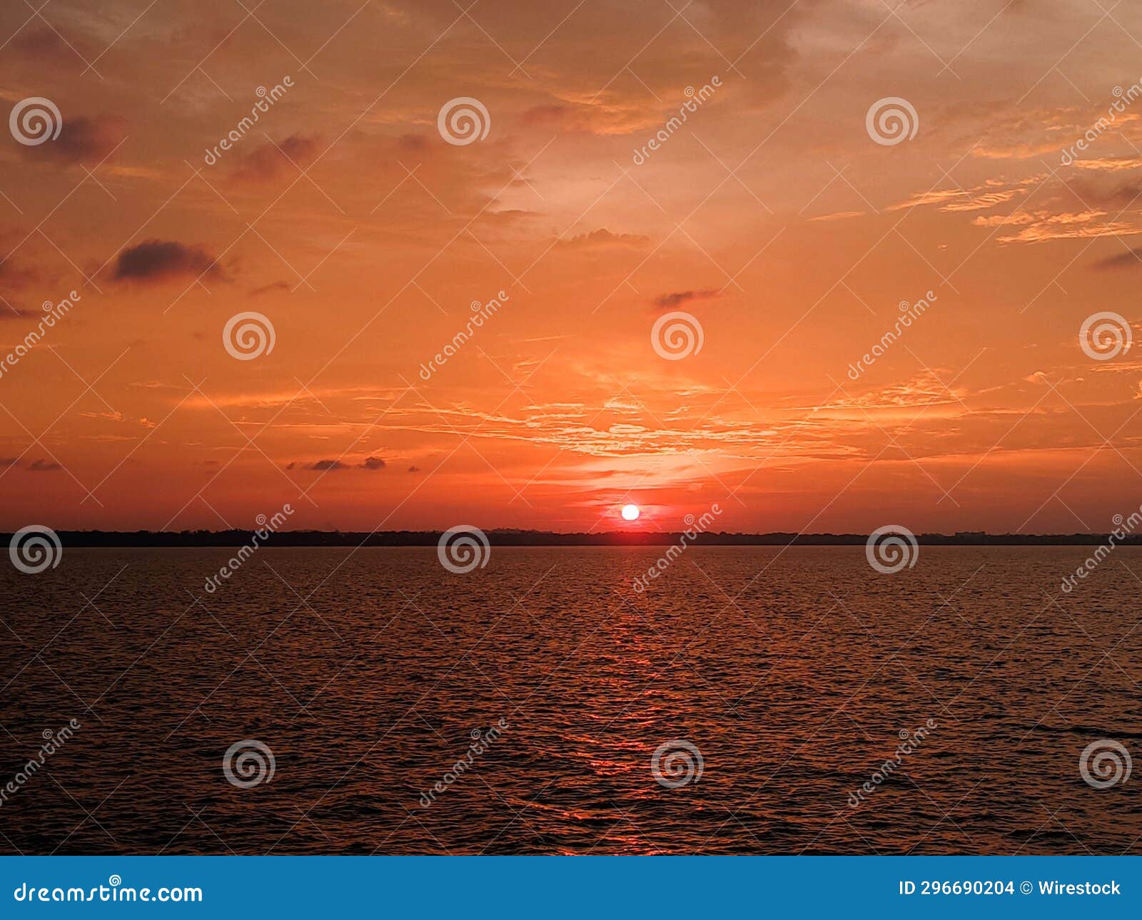 A Red Sun Setting Over the Ocean with Clouds in the Sky Stock Photo ...