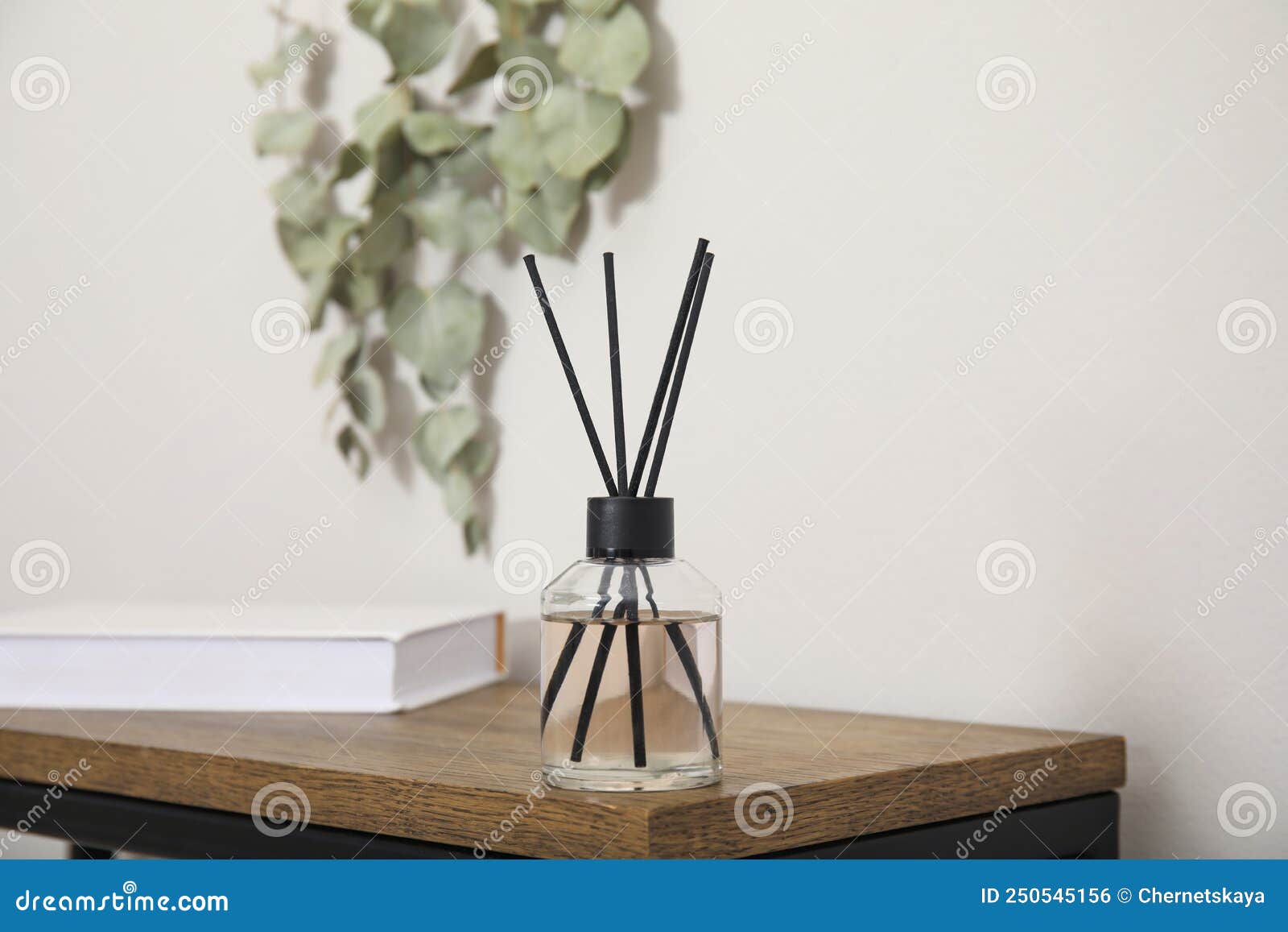 Reed Diffuser and Book on Wooden Table Near White Wall Stock Photo ...
