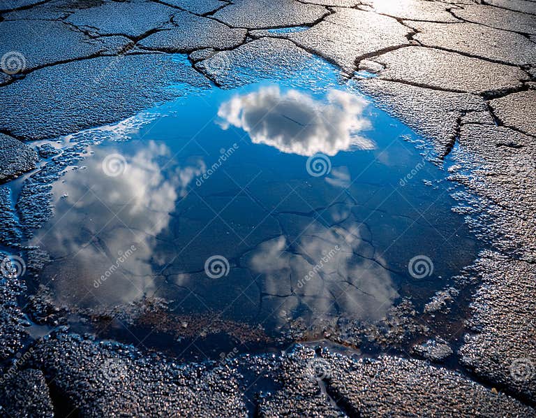 Reflection of Blue Sky and Clouds in Puddle on Cracked Pavement with ...