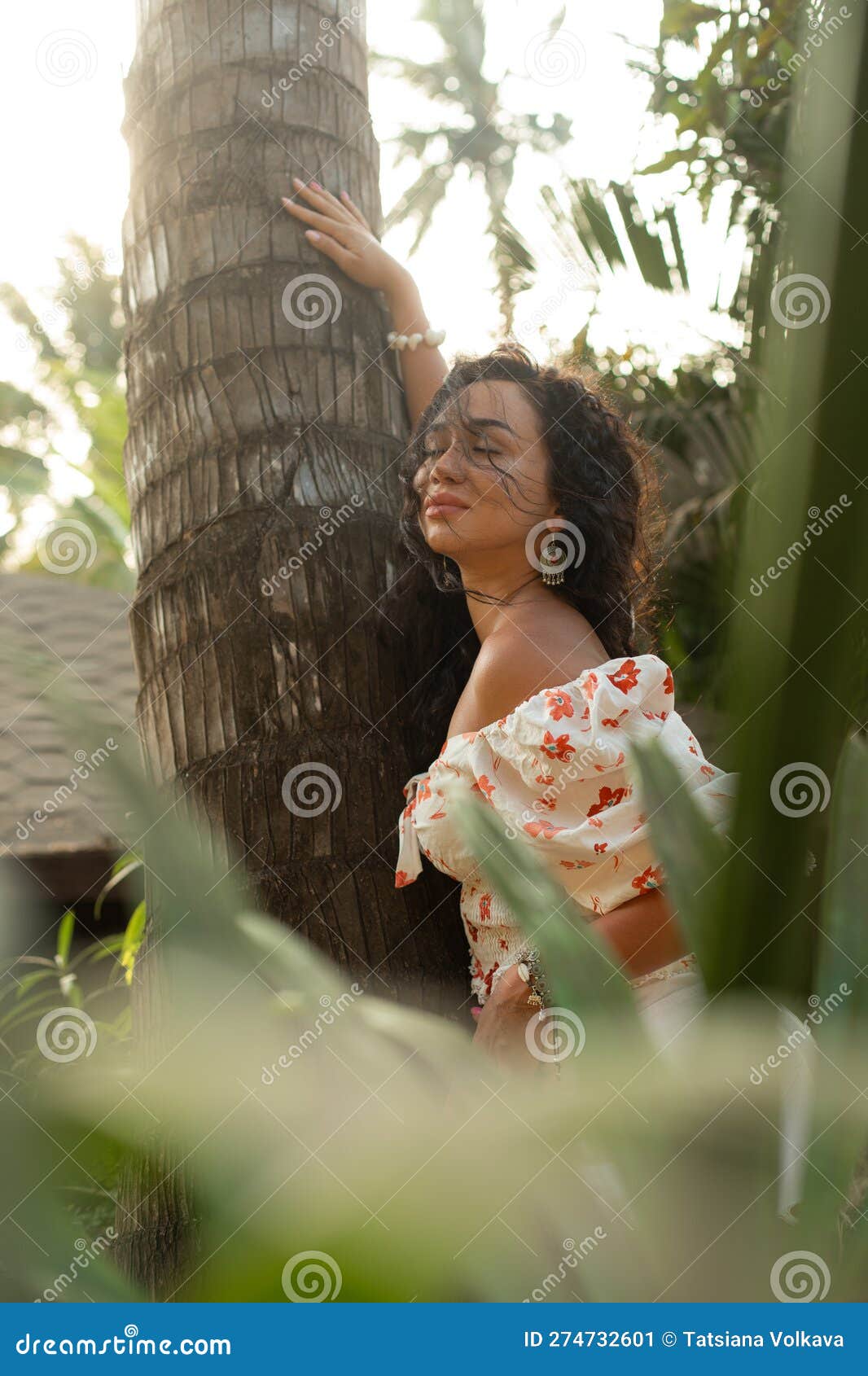 Relaxed Curly Haired Female Leaning On Palm Tree Trunk With Close Eyes