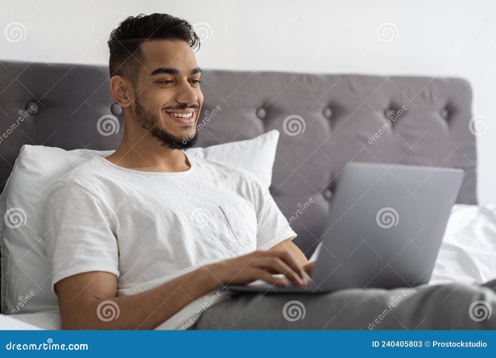 Remote Work. Handsome Young Arab Man Using Laptop while Sitting in Bed ...