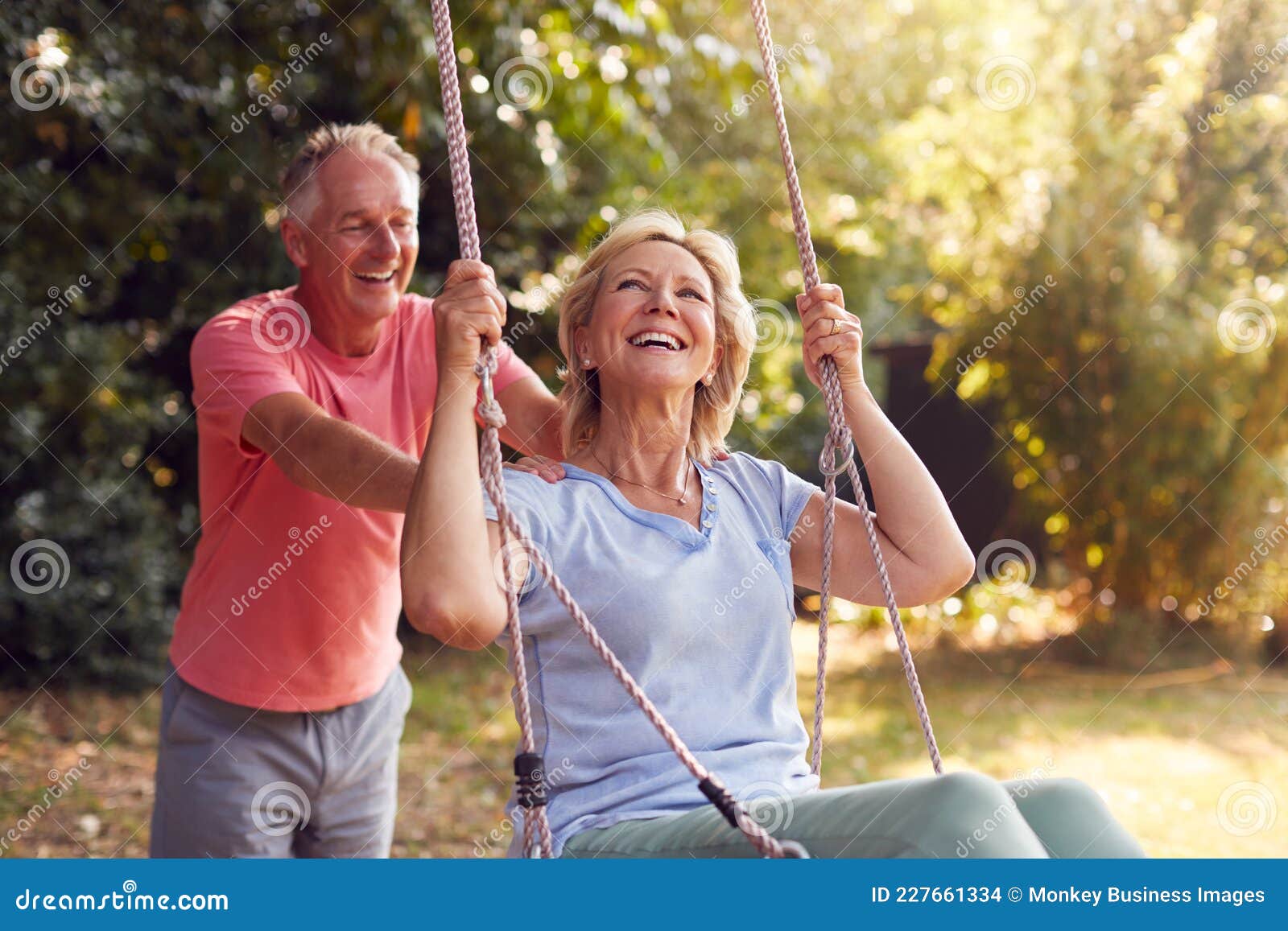 Retired Couple Having Fun With Man Pushing Woman On Garden Swing Stock