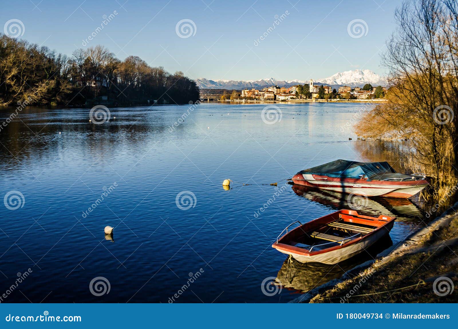 River with Small Boats and Small Village in Front of the Alps Stock ...