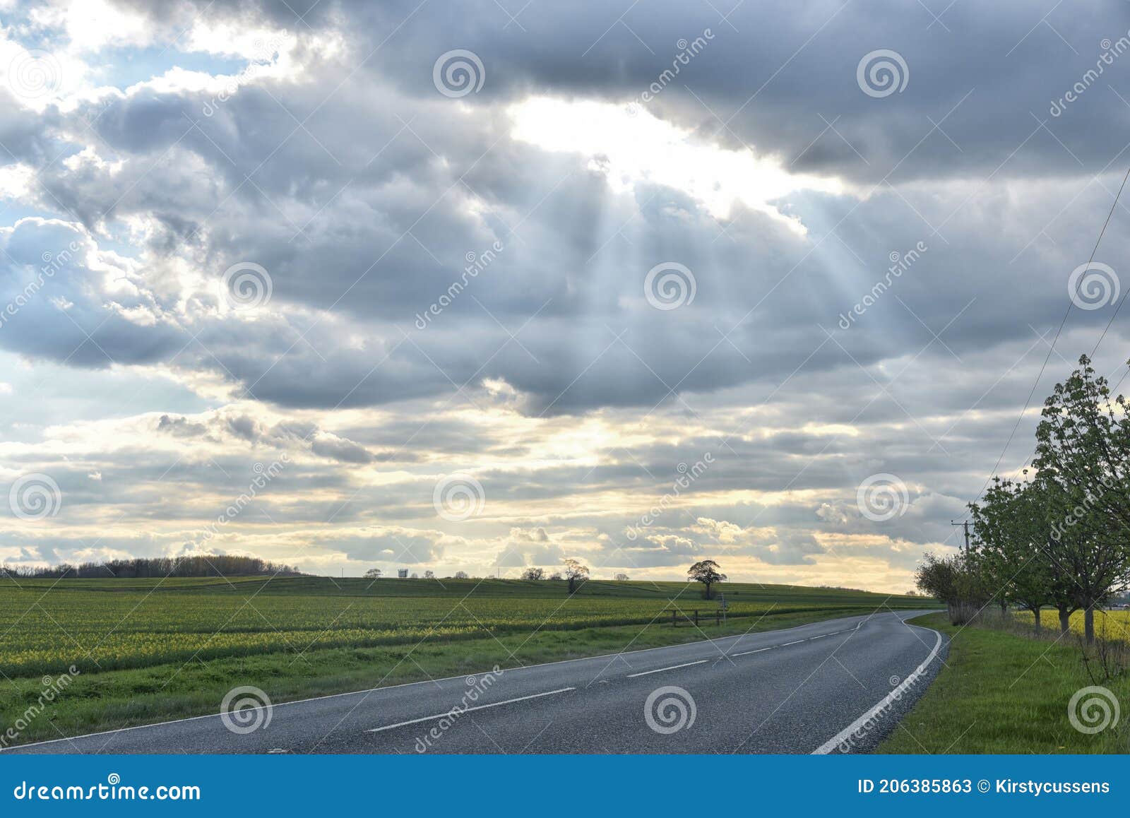 Road Going into the Distance beside Fields and Under a Cloudy Sky with ...