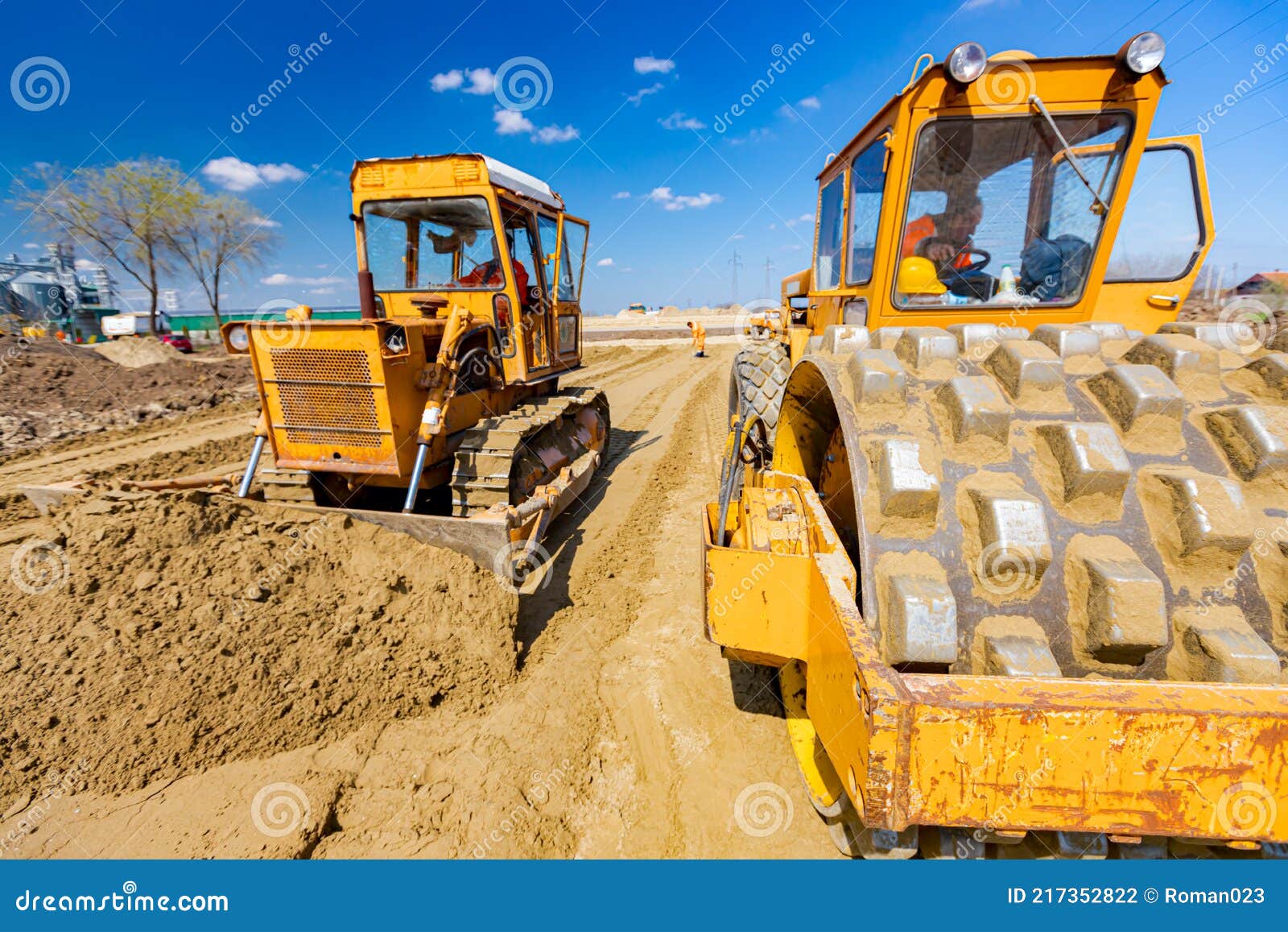 Road Roller with Spikes and Earthmover are Working at Construction Site ...