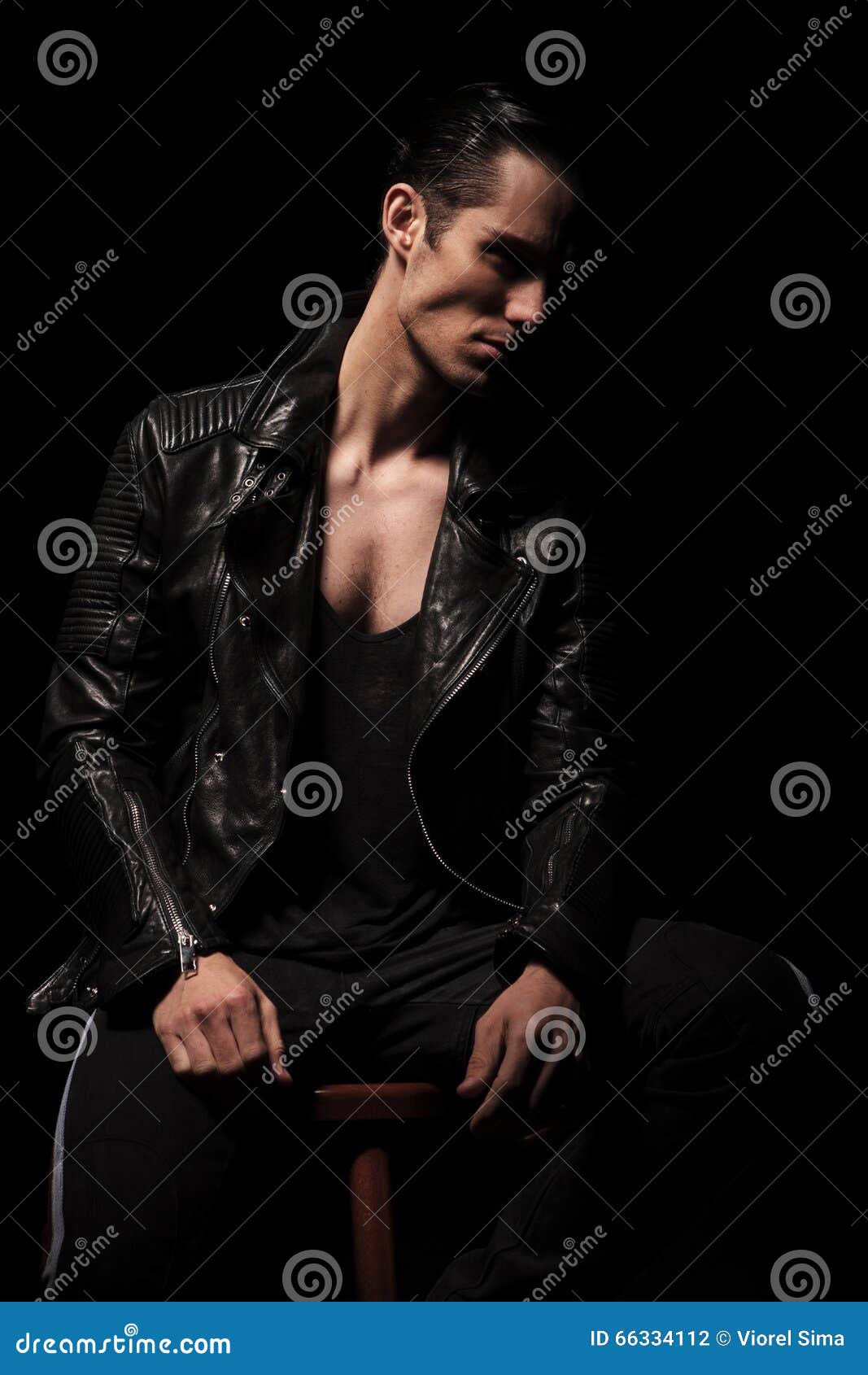 Rocker In Black Leather Jacket Posing Seated In Dark Studio Stock Photo ...
