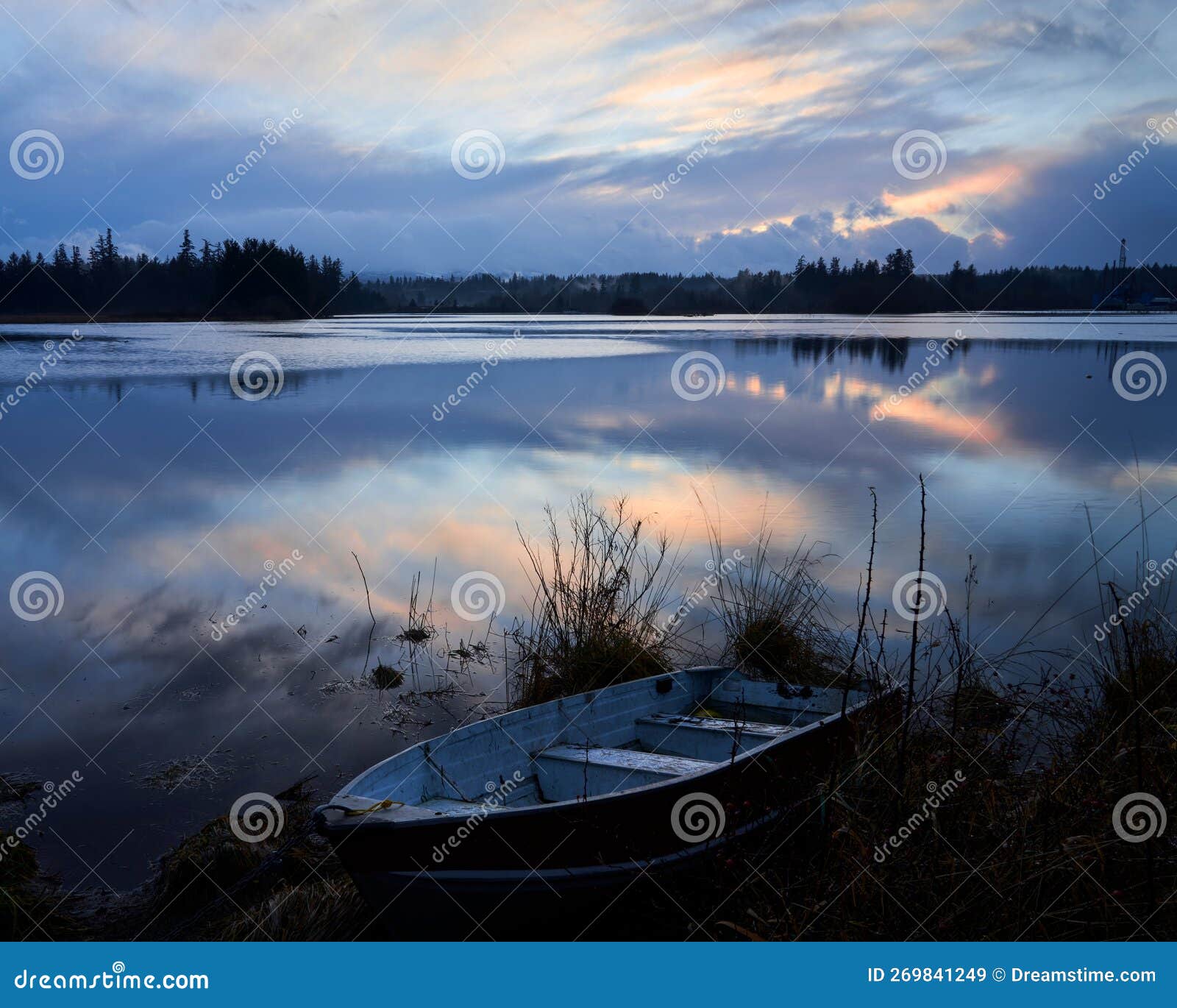 Silhouette of a Row Boat on the Shore at Dusk with Cloud Reflections in ...