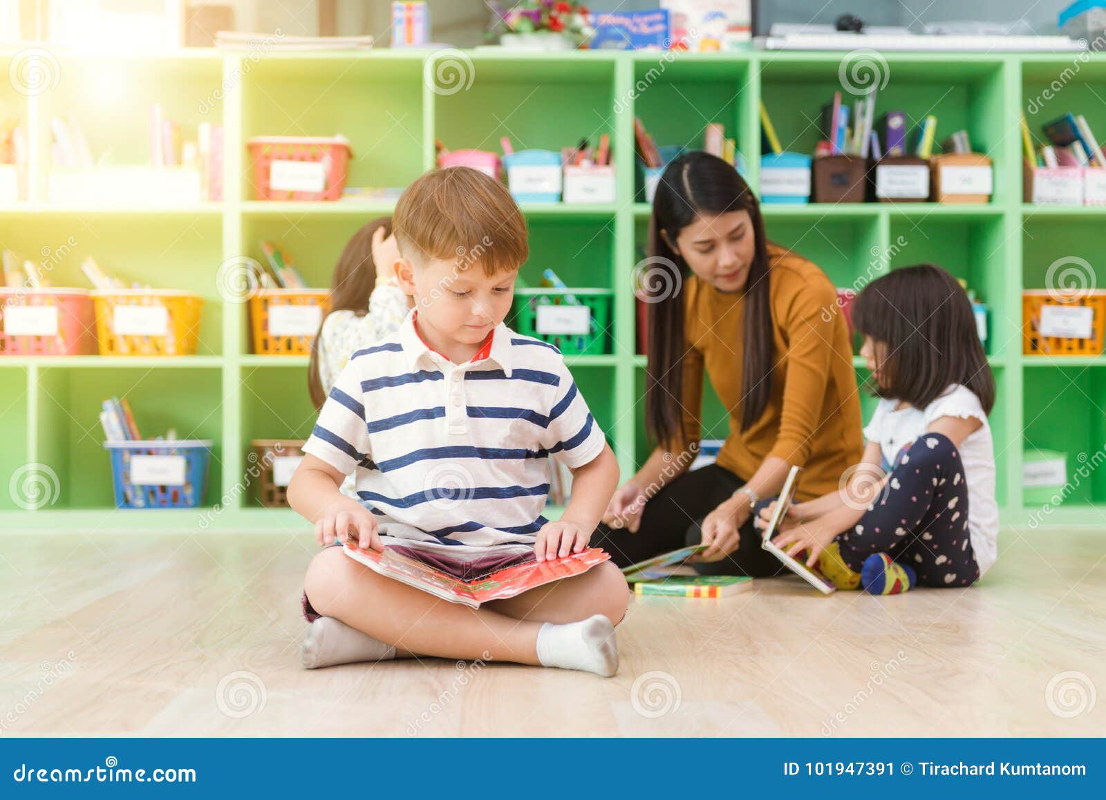 Row Of Multiethnic Elementary Students Reading Book In Classroom ...