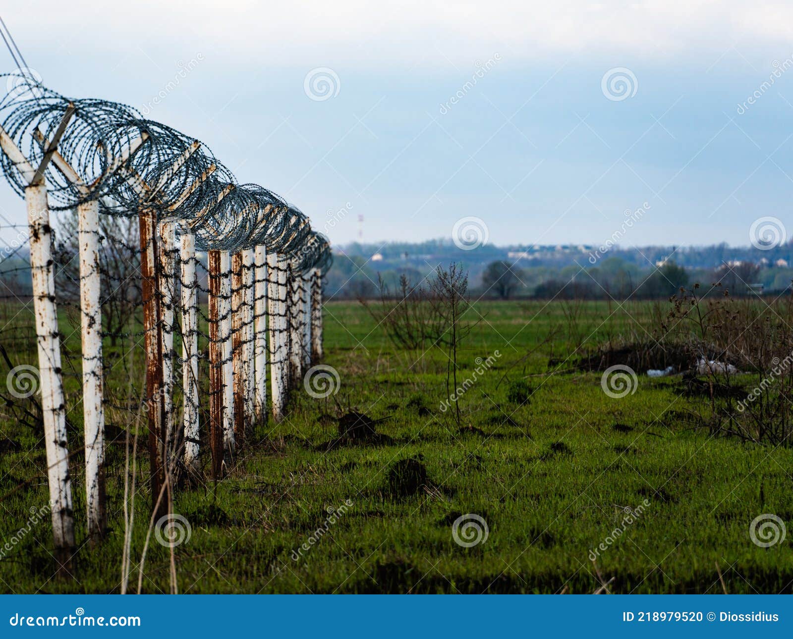 A Rusty Fence with Barbed Wire Stands in a Green Field Stock ...