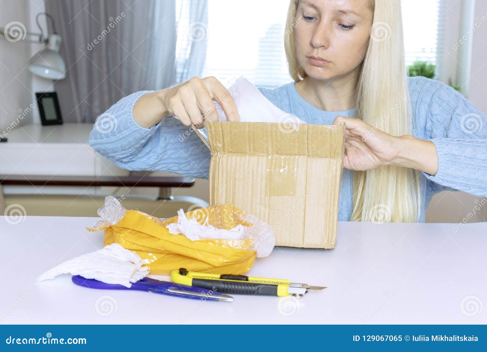 Sad Blond Woman Sitting by the Table and Opening a Box, Unboxing a ...
