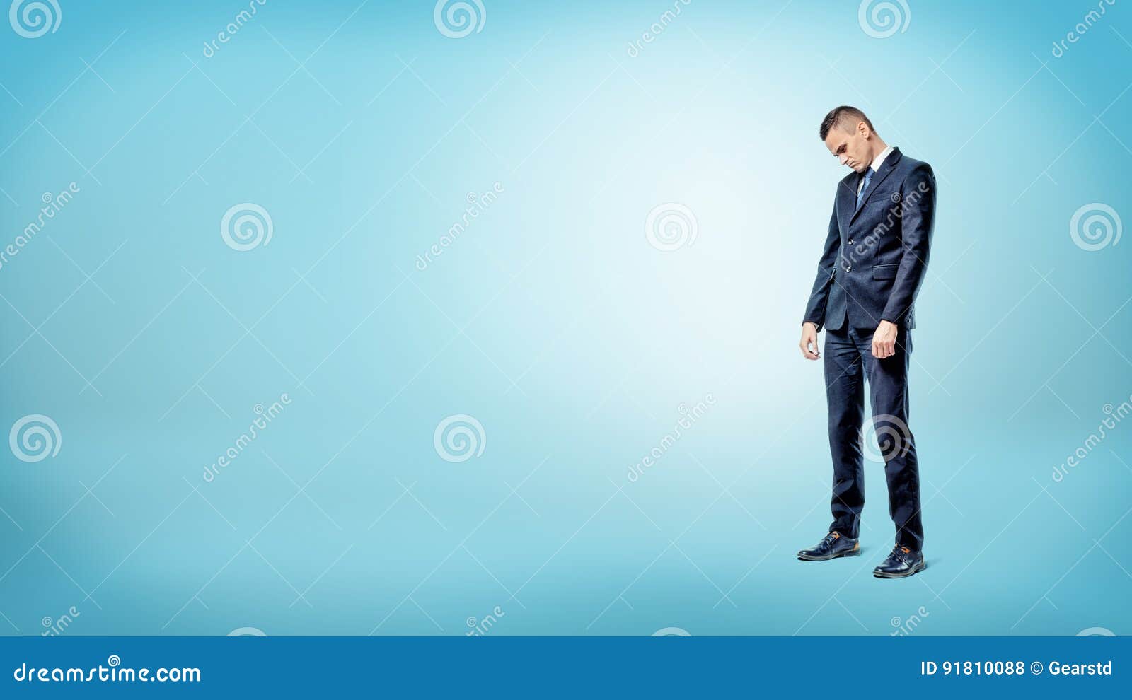 A Sad Businessman Standing on Blue Background Looking Down with Slumped ...