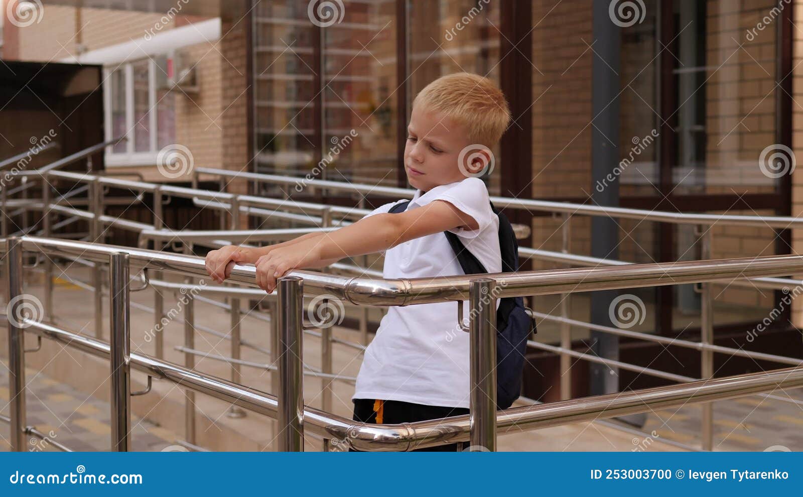 A Sad Little Boy with a Backpack is Standing Alone in the School Yard ...