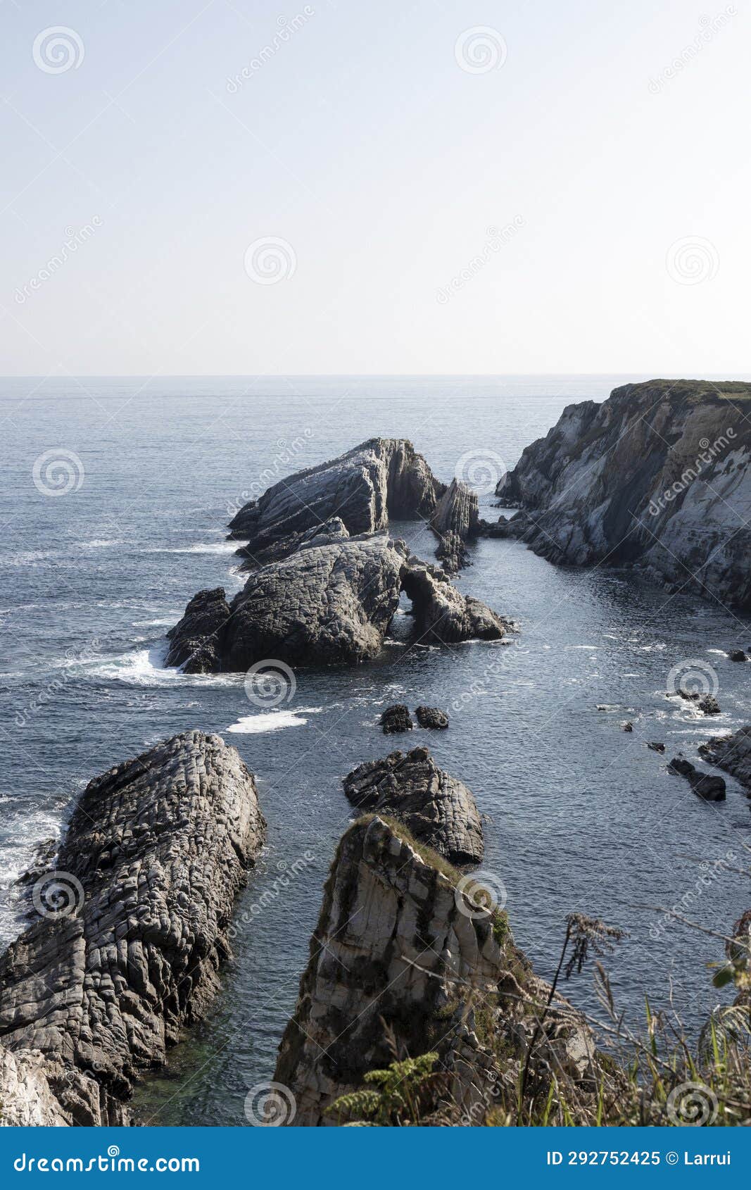 Sunlit Scene of Jagged Rocks and Ocean Under a Light Blue Sky Stock ...