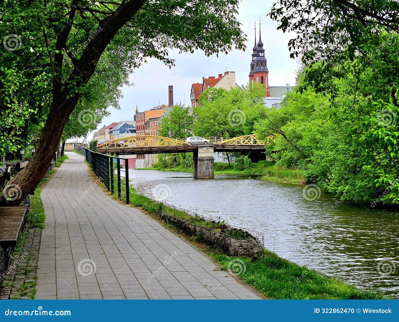 Scenic Pathway by the River with a Bench and Bridge in the Distance ...