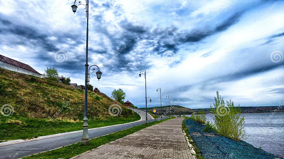 Scenic Riverside Walkway with Lamp Posts and Dramatic Clouds in Early ...