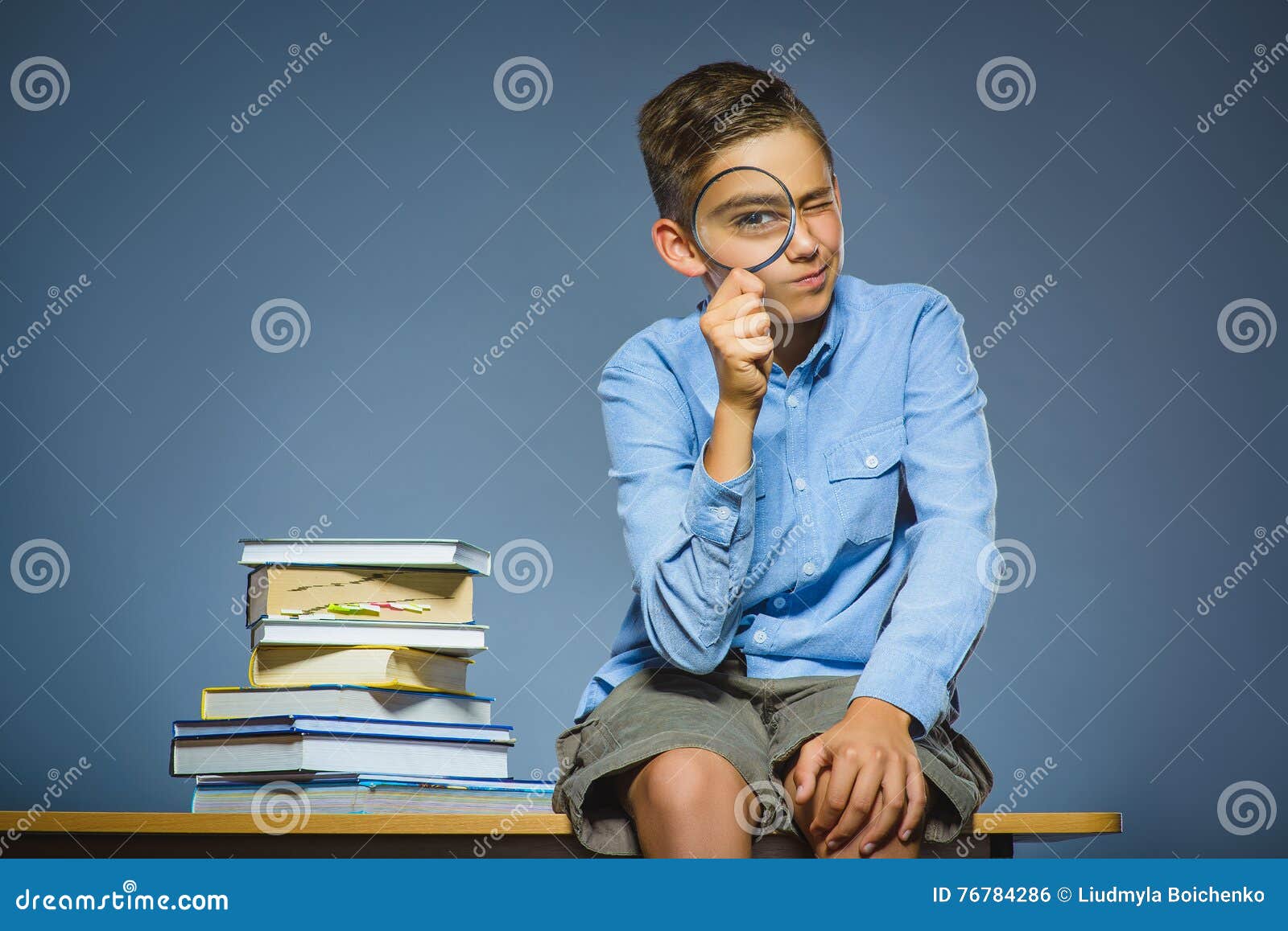 School Concept. Doubt Boy Sitting on Desk and Looking into a Magnifying ...