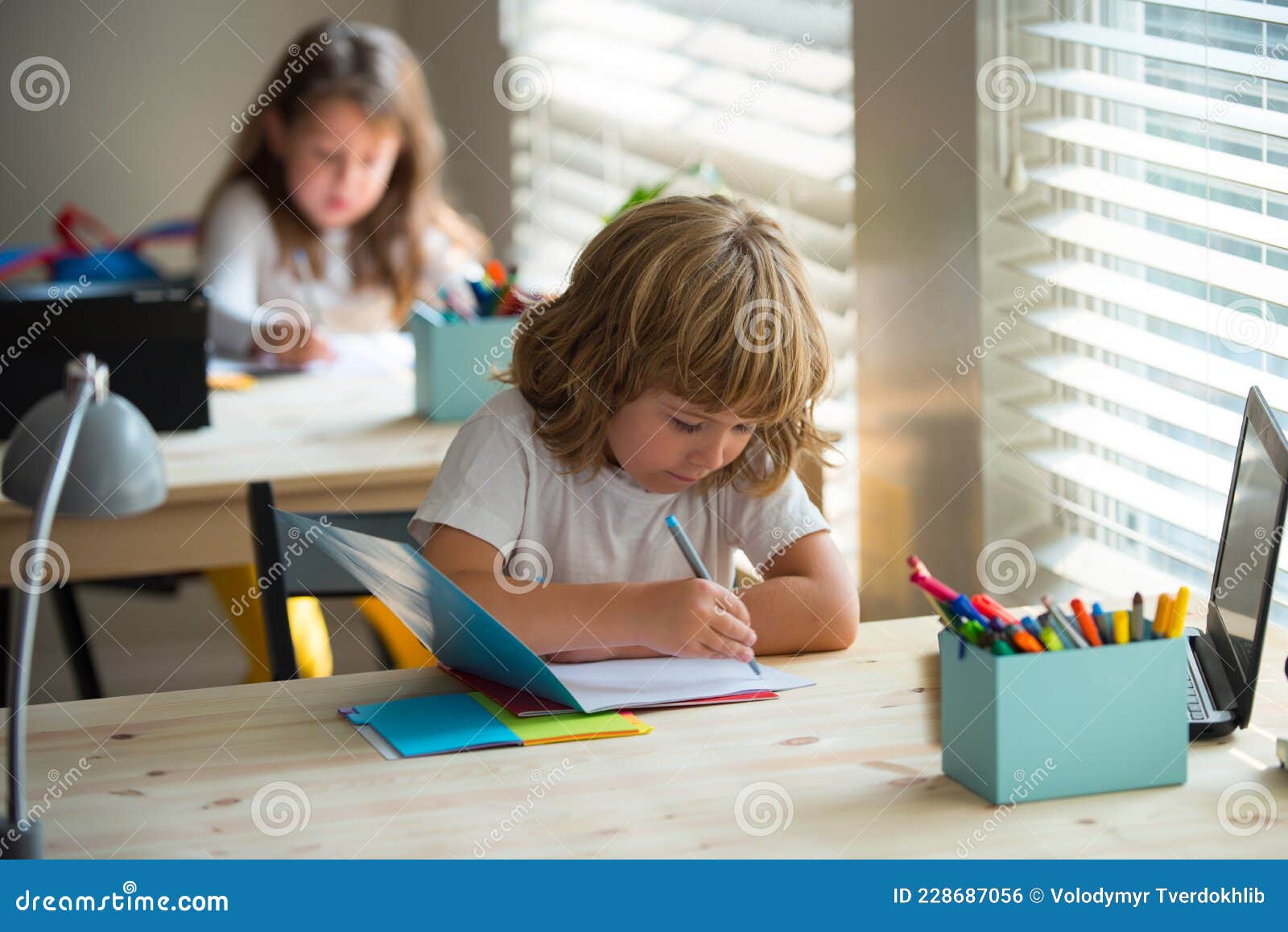 School Kid Writing Something in Copybook and Sitting at Table in ...
