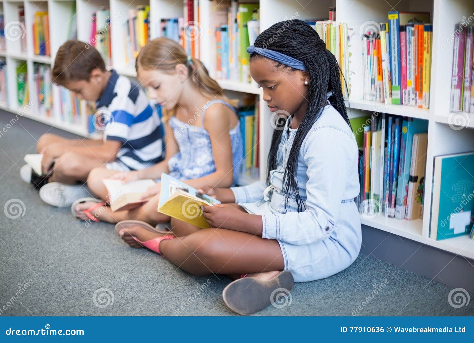 School Kids Sitting on Floor and Reading Book in Library Stock Photo ...