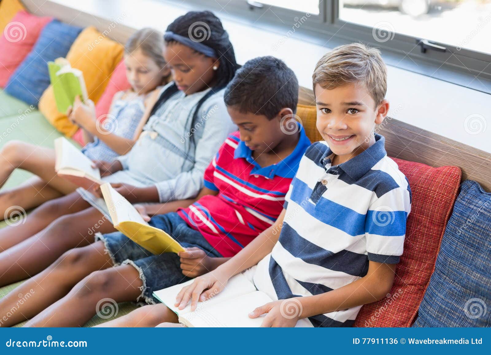 School Kids Sitting on Sofa and Reading Book in Library Stock Photo ...