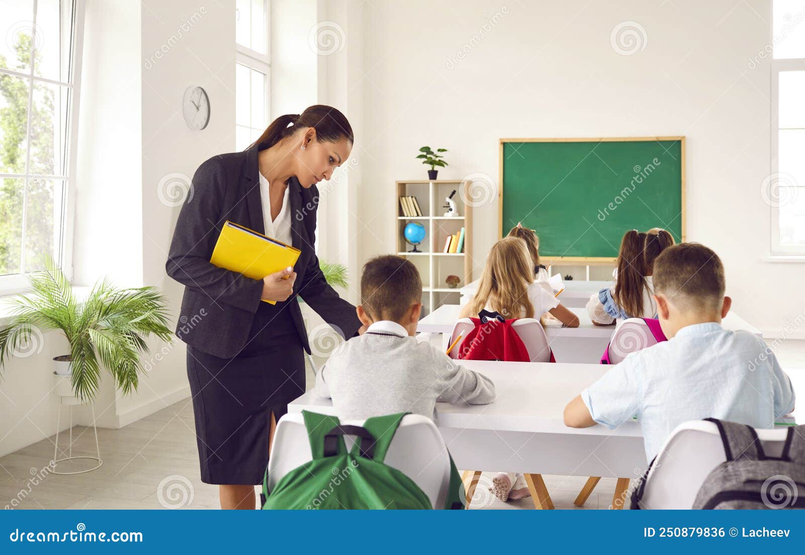 School Teacher Helping Her Elementary Students Who are Sitting at Desks ...