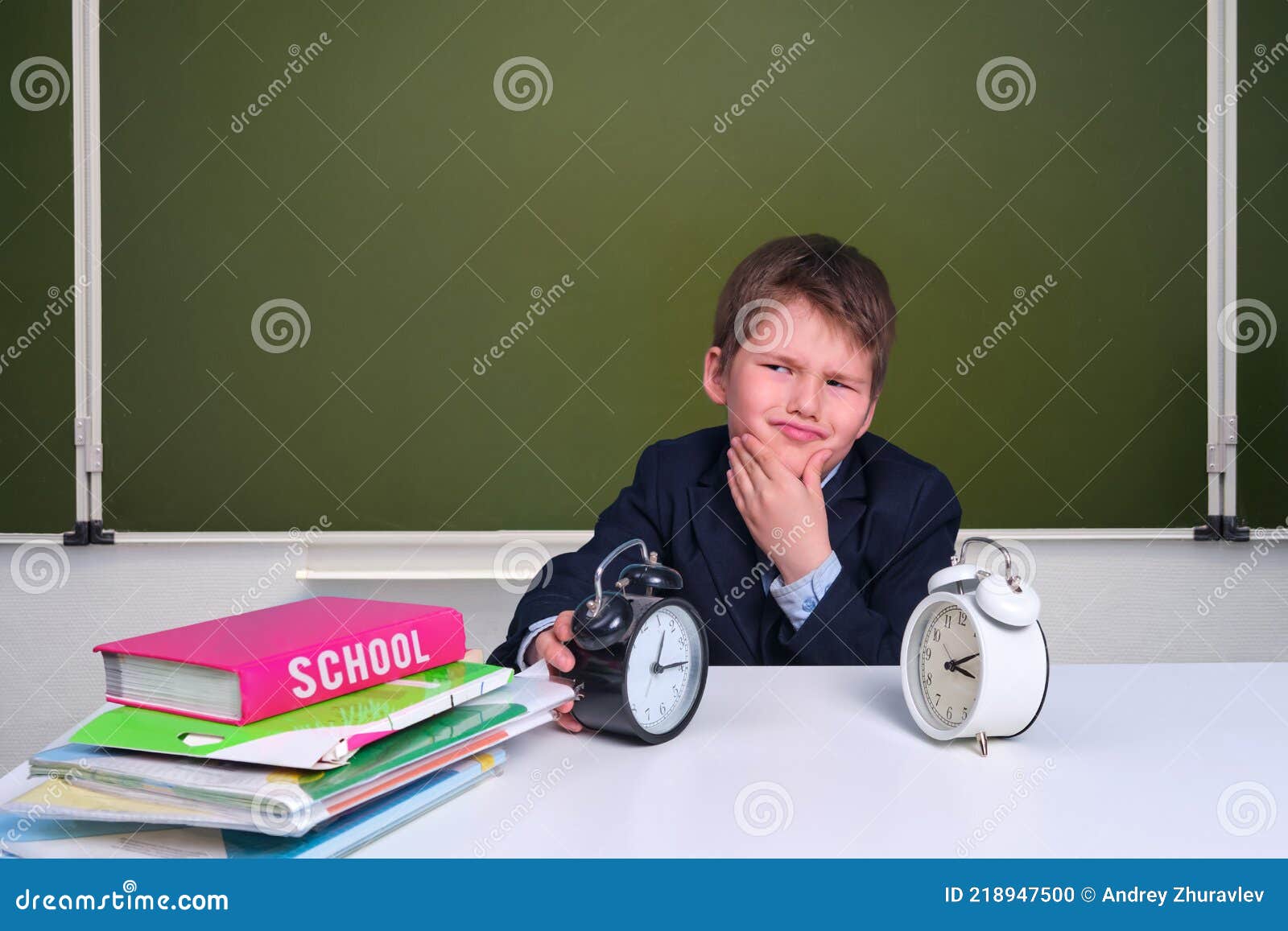 Schoolboy Boy with Alarm Clock in Hands at the Table in School Class ...