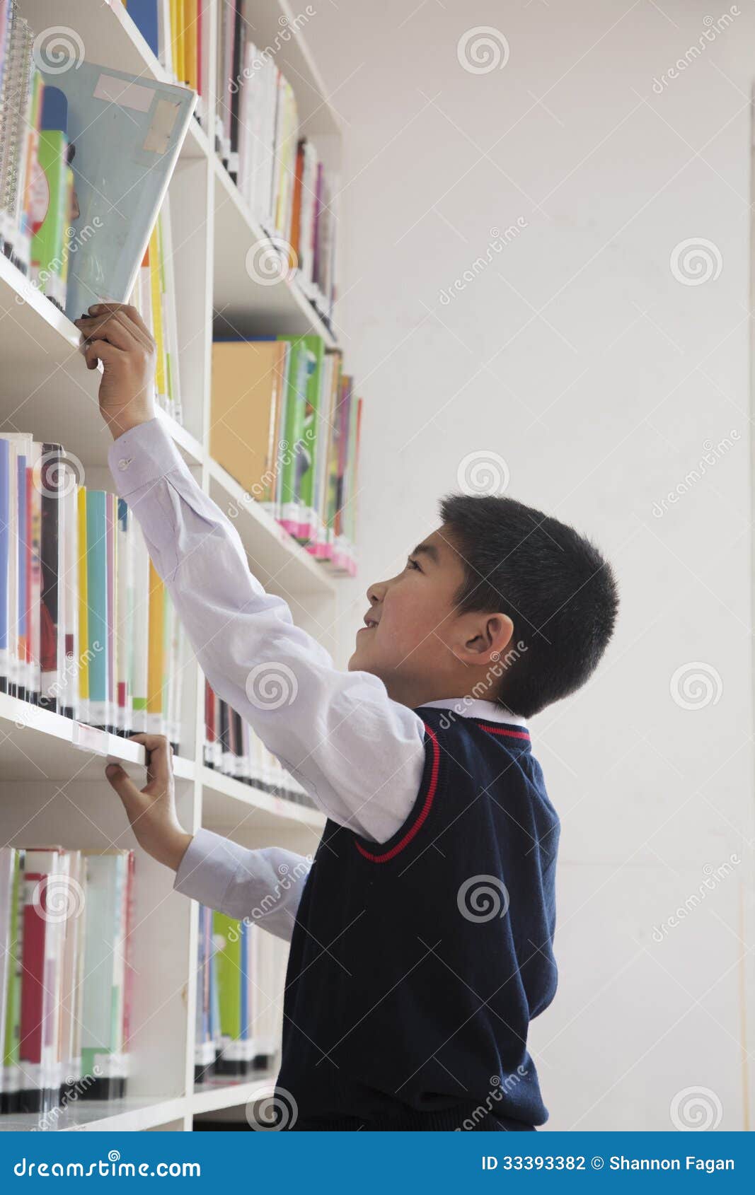 Schoolboy Reaching for Book Off Bookshelf Stock Photo - Image of ...