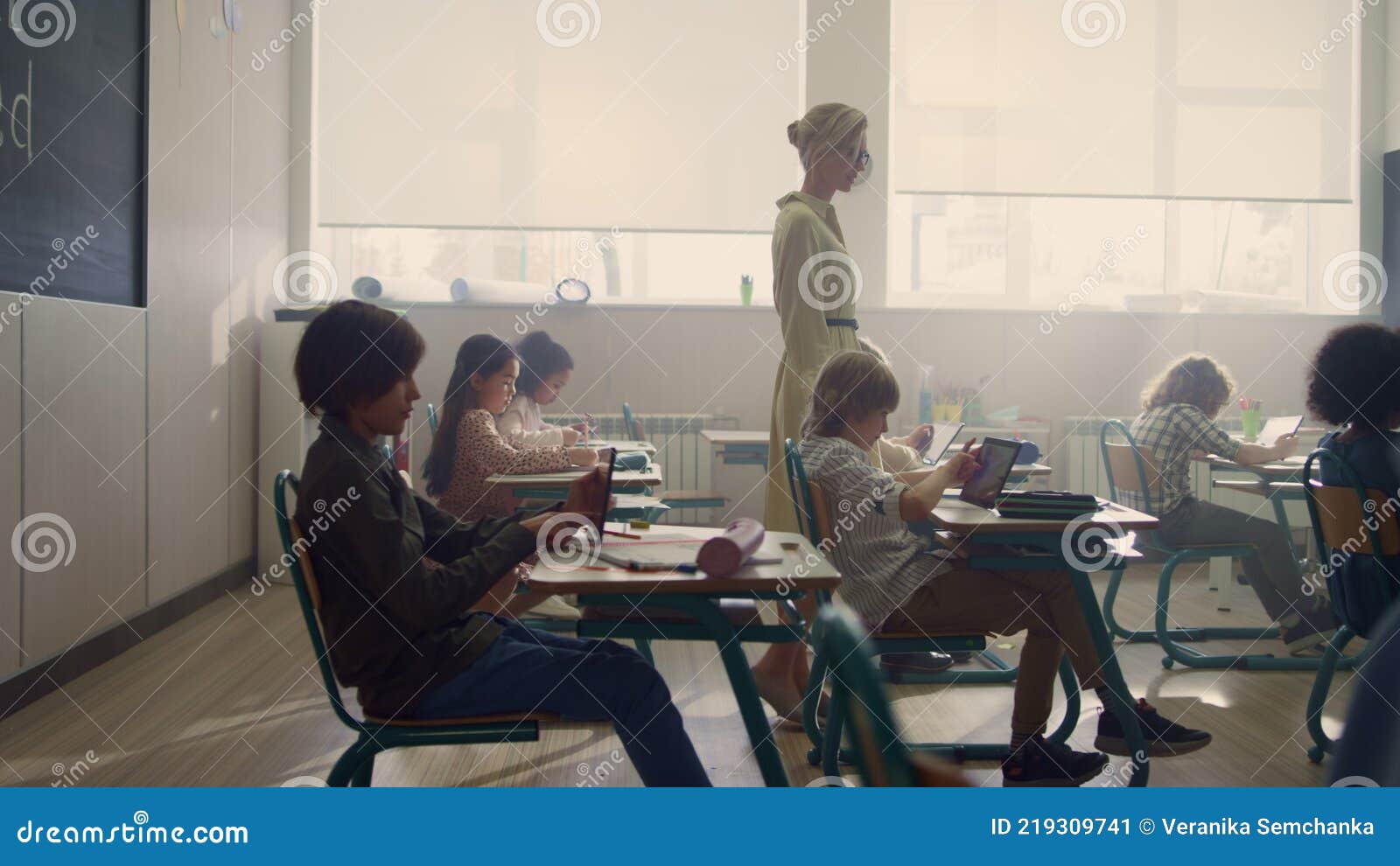 Schoolteacher Walking in Classroom with Students. Pupils Doing Test on ...