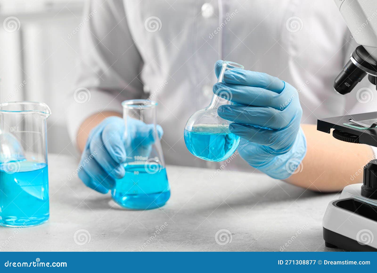 Scientist with Flasks of Light Blue Liquid at White Table in Laboratory ...