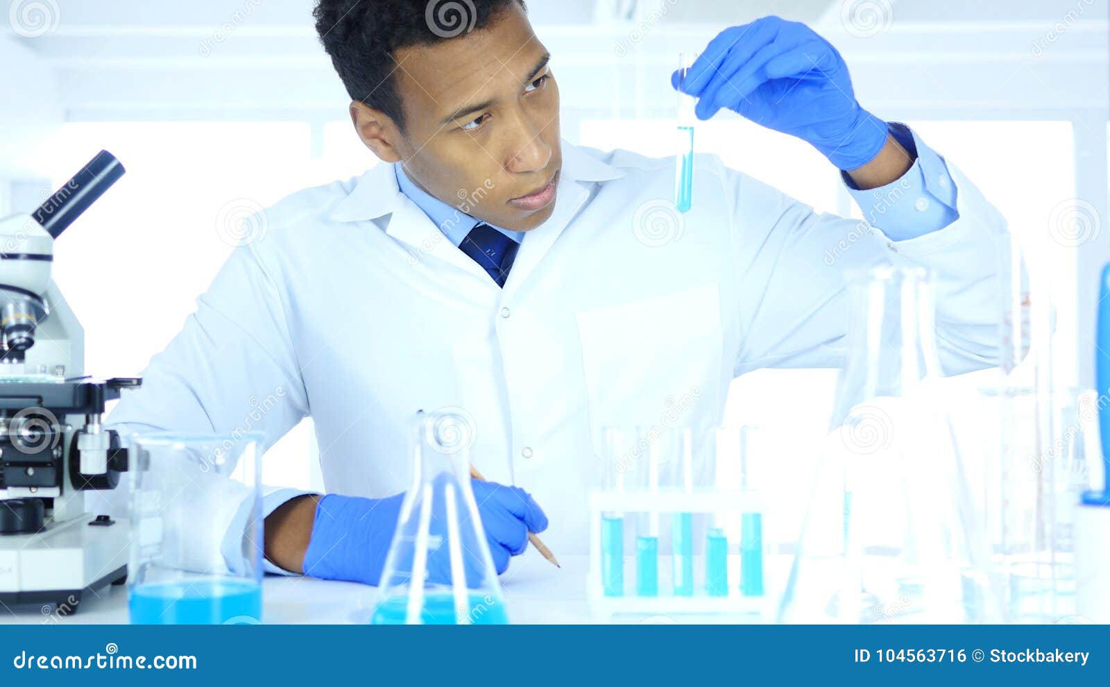 Scientist Looking at Test Tube Blue Solution and Using Microscope in ...