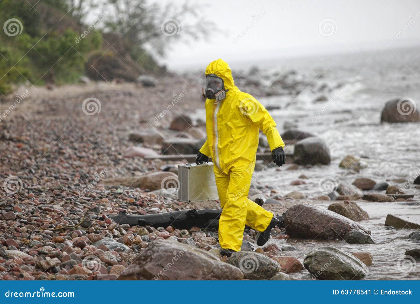 Scientist in Protective Suit with Silver Case Walking in on Rocky Beach ...