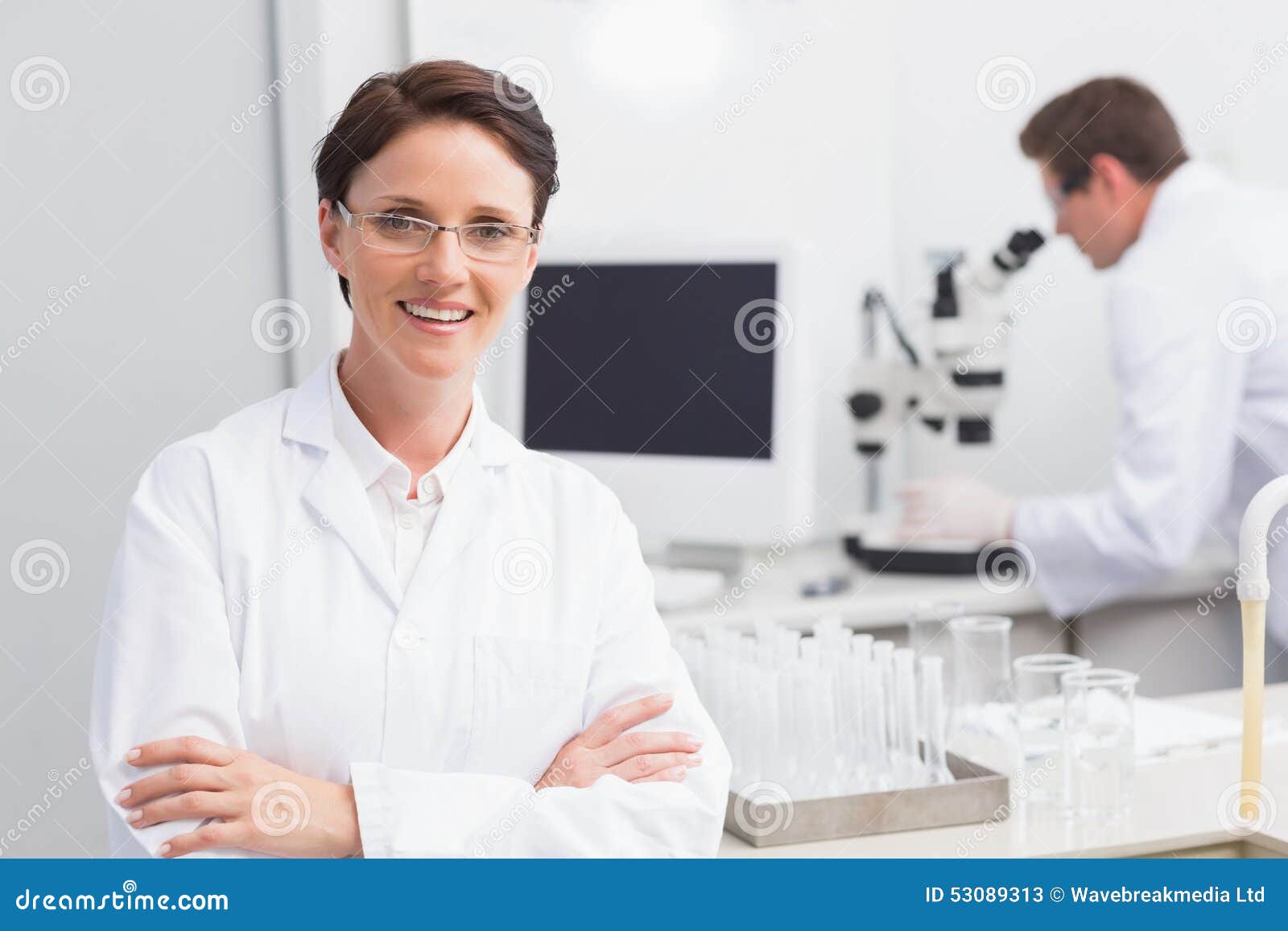 Scientist Smiling at Camera Arms Crossed and Another Working with ...