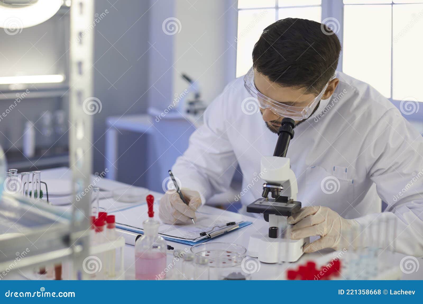 Scientist Taking Notes Sitting at Table with Microscope in Microbiology ...