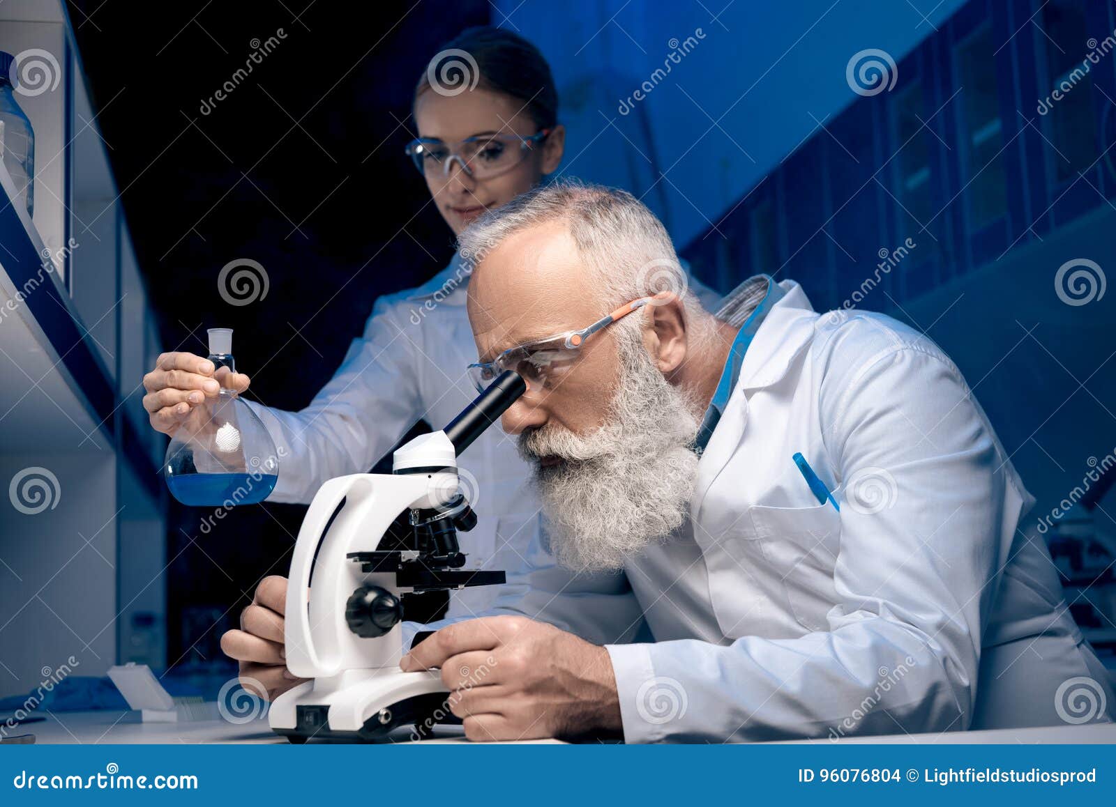 Scientist Using Microscope while Colleague Holding Reagent in Tube ...