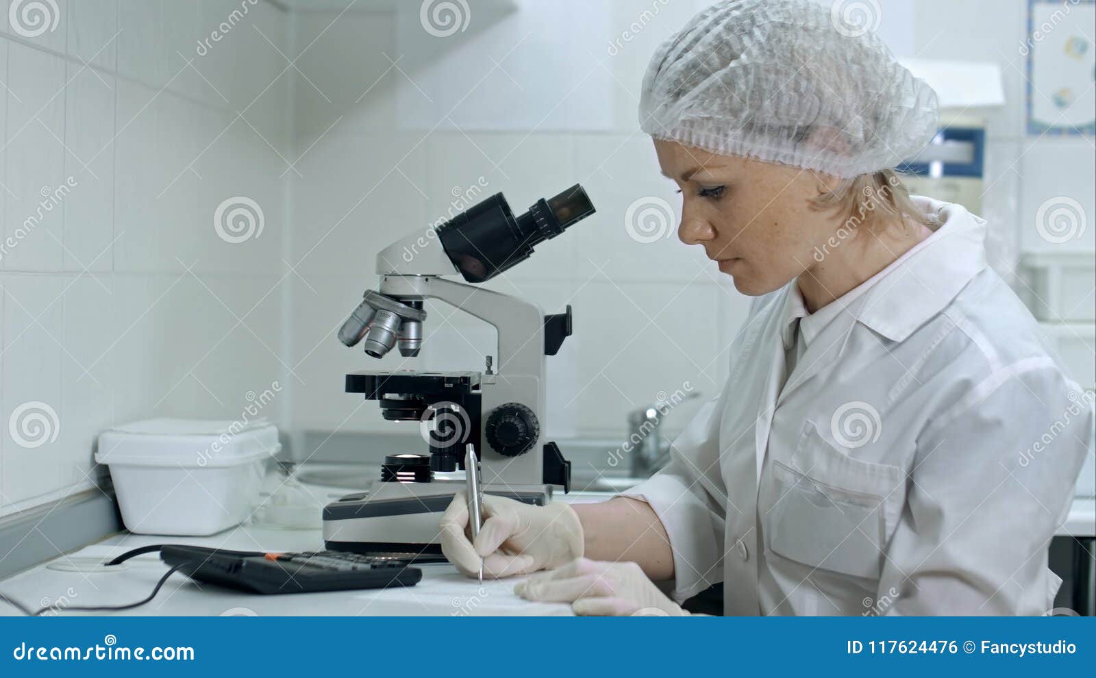 Scientist Working with Microscope, Calculating and Taking Notes in ...