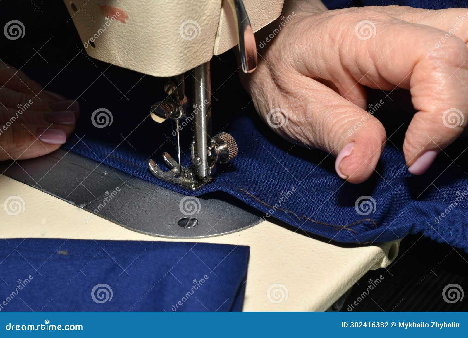 The Seamstress Uses Her Hand To Help the Fabric Move Under the Needle ...