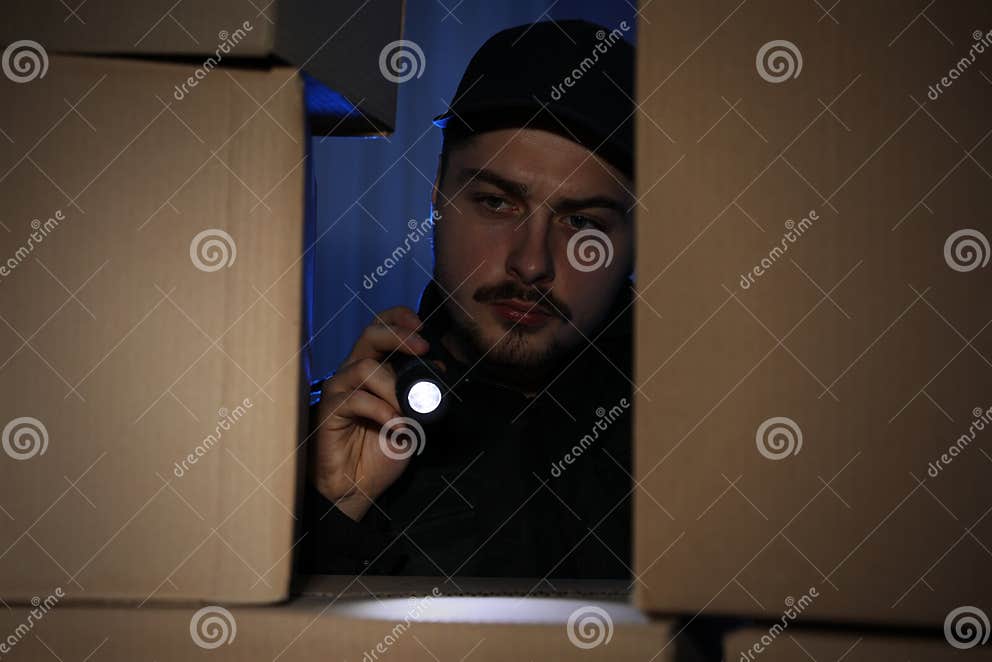 Security Guard with Flashlight Looking through Pile of Cardboard Boxes ...
