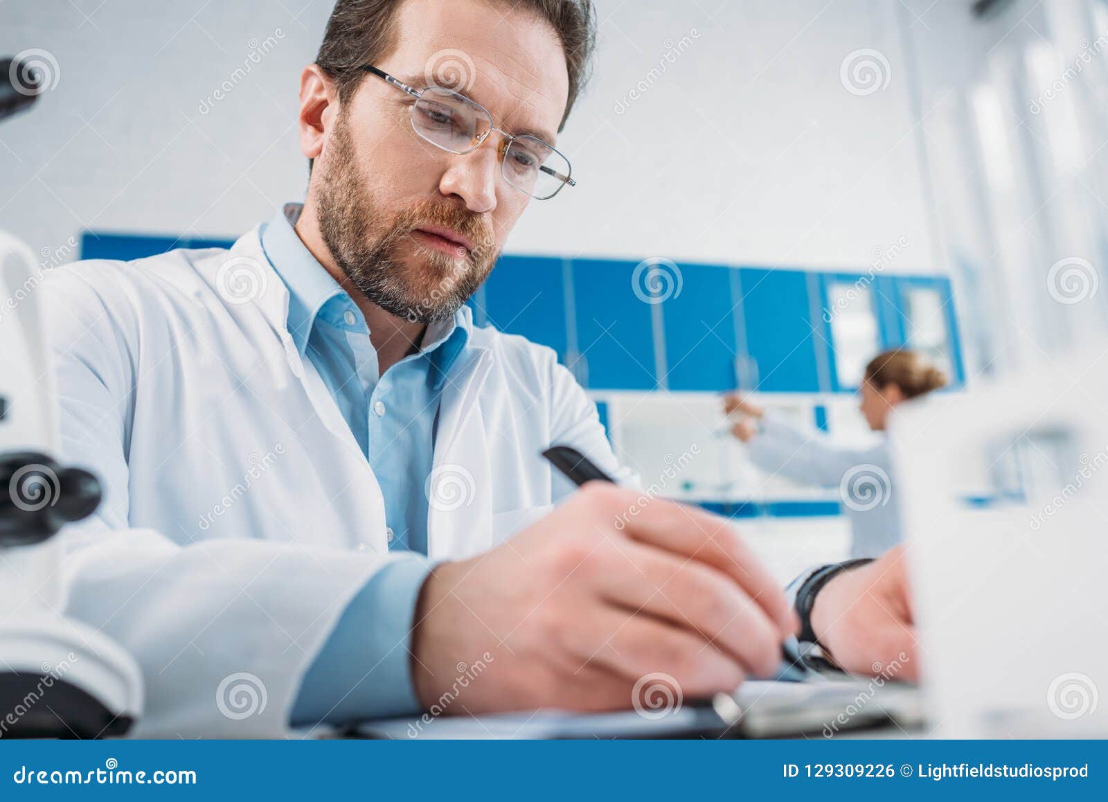 Selective Focus of Scientist in White Coat and Eyeglasses Making Notes ...