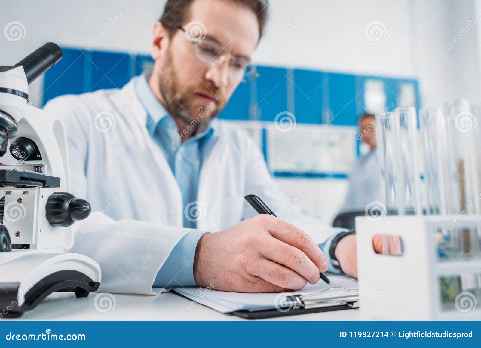 Selective Focus of Scientist in White Coat and Eyeglasses Making Notes ...