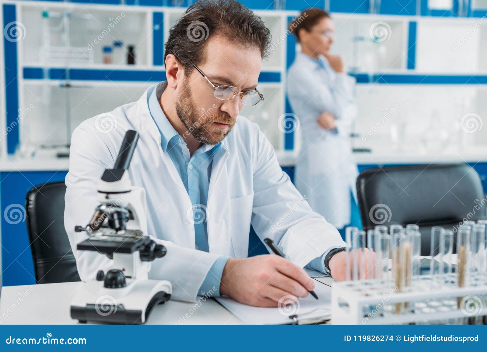 Selective Focus of Scientist in White Coat and Eyeglasses Making Notes ...