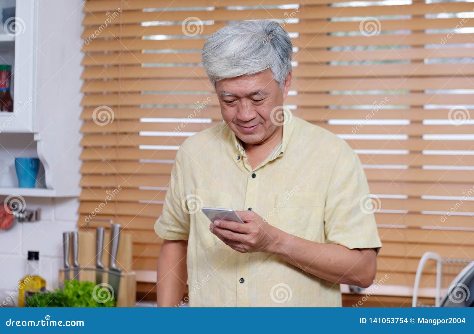 Senior Asian Man Using Smart Phone while Standing in Kitchen at Home ...
