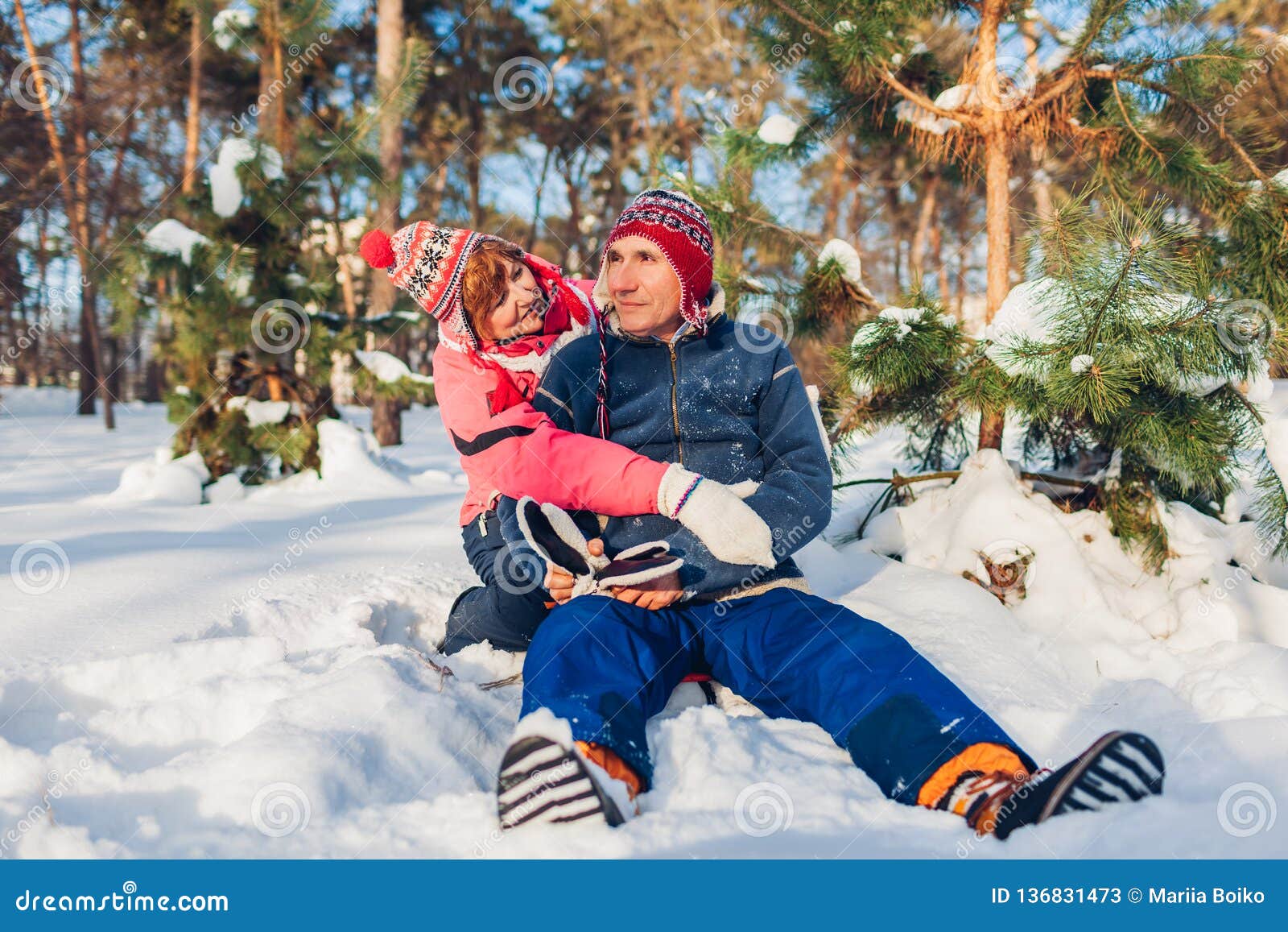 Senior Couple Hugging In Winter Forest Man And Woman Sitting In Snow