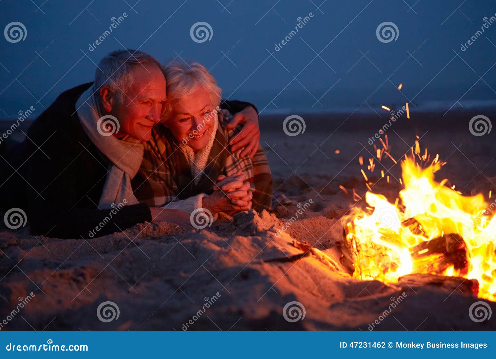 Senior Couple Sitting by Fire on Winter Beach Stock Photo - Image of ...