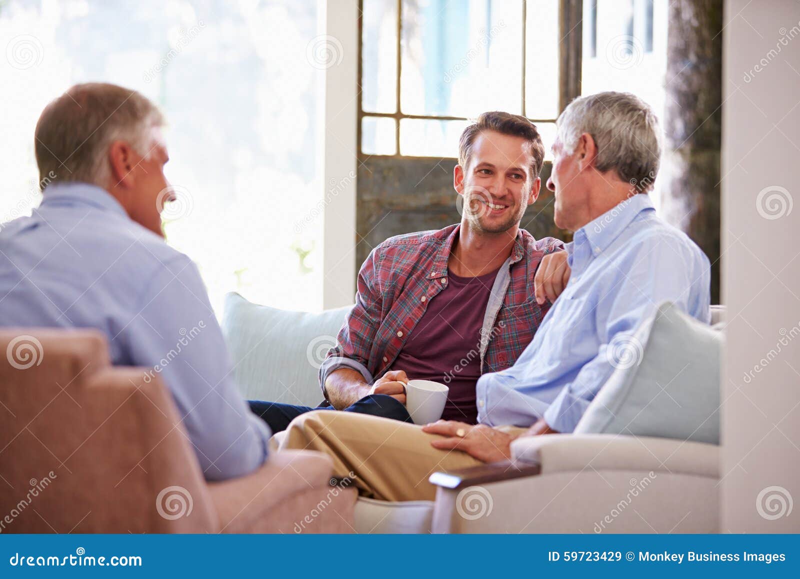 Senior Father With Adult Son Relaxing On Sofa At Home Stock Image