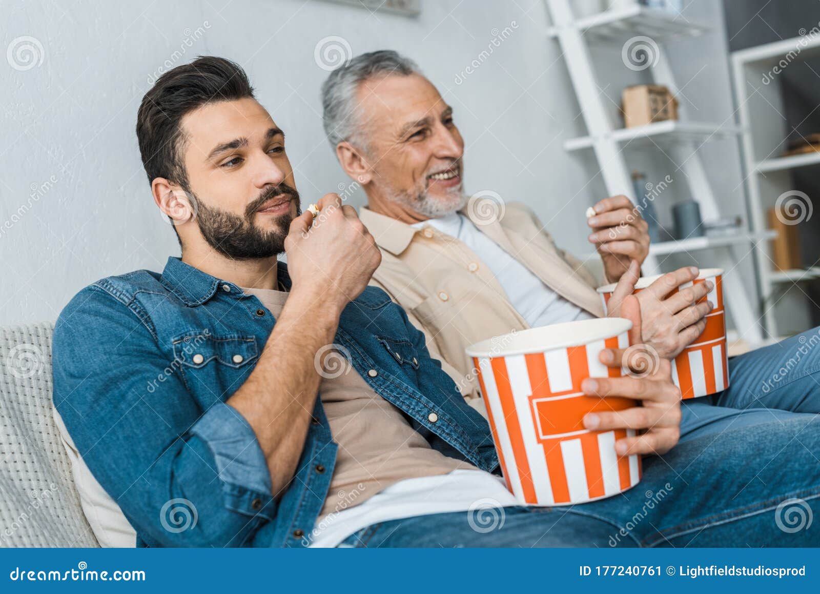 Senior Father Sitting With Handsome Son And Holding Popcorn Bucket