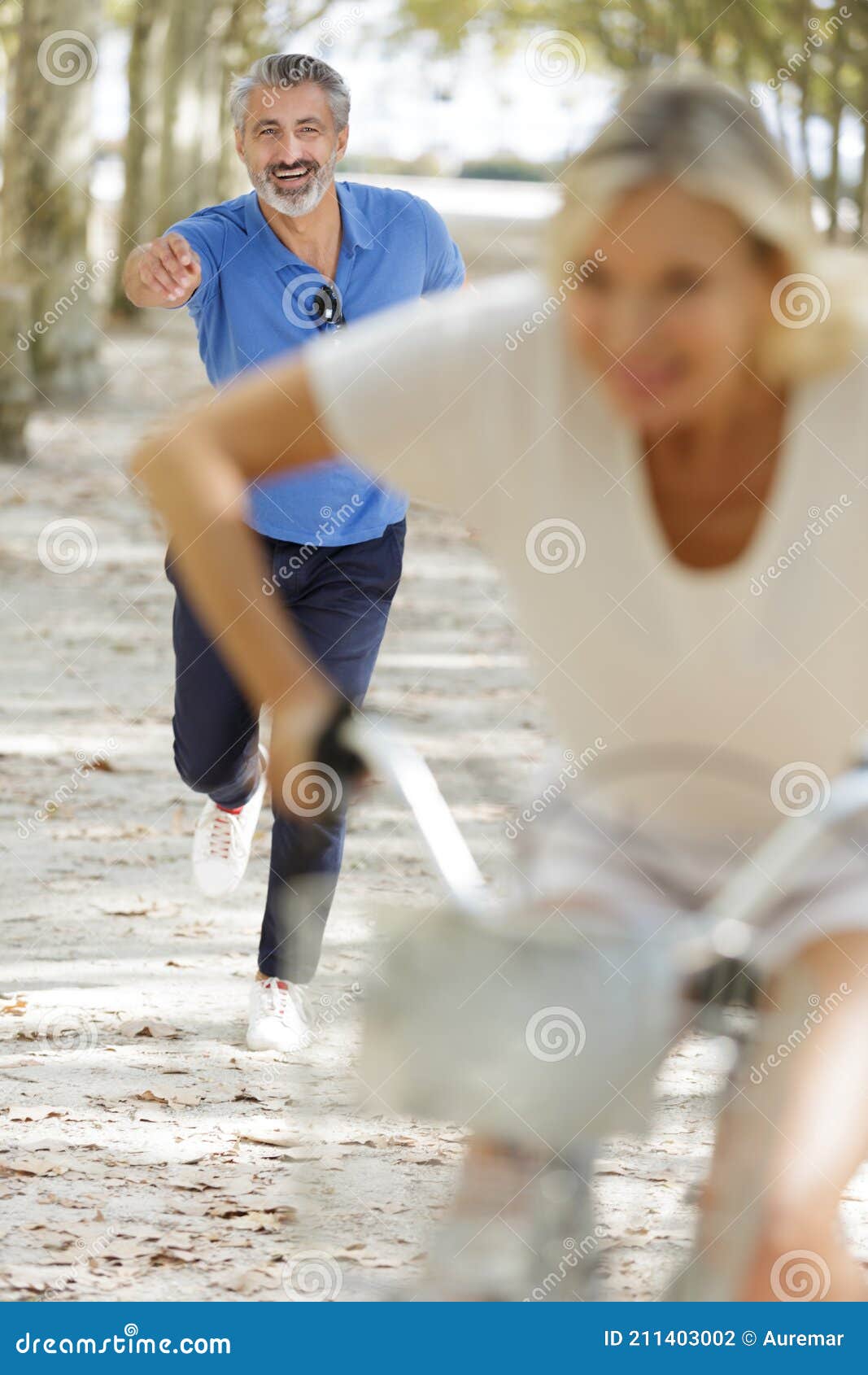 Senior Man Playfully Chasing Woman on Bicycle Stock Photo - Image of ...