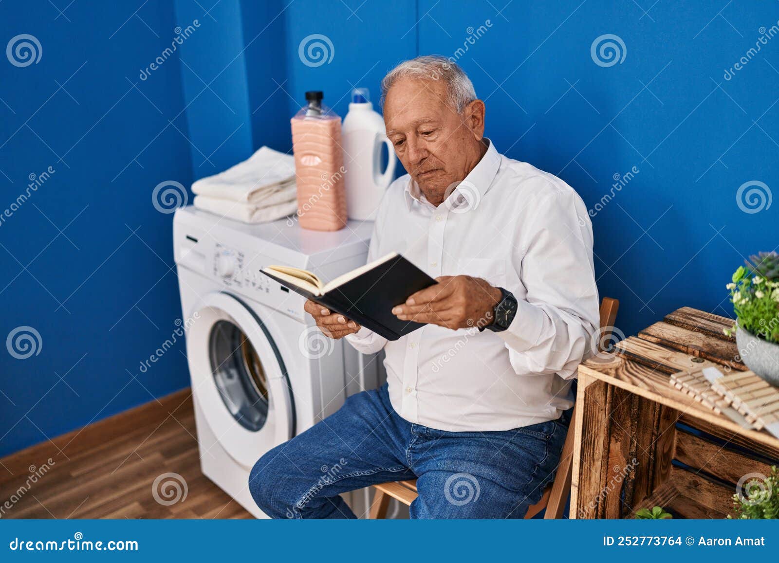 Senior Man Reading Book Waiting for Washing Machine at Laundry Room ...