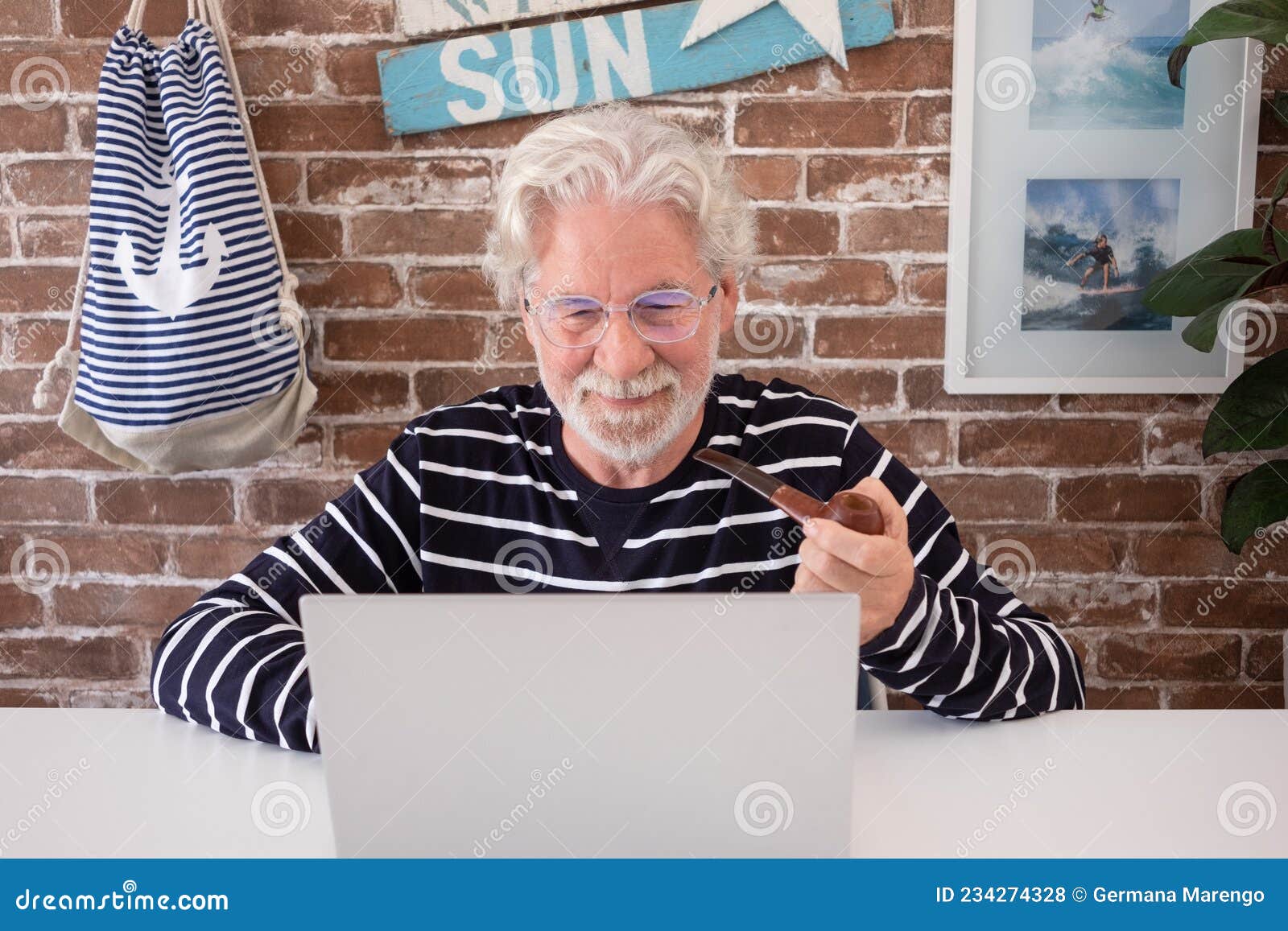 Senior Man Smoking Pipe while Using Laptop Computer at Home. Brick Wall ...