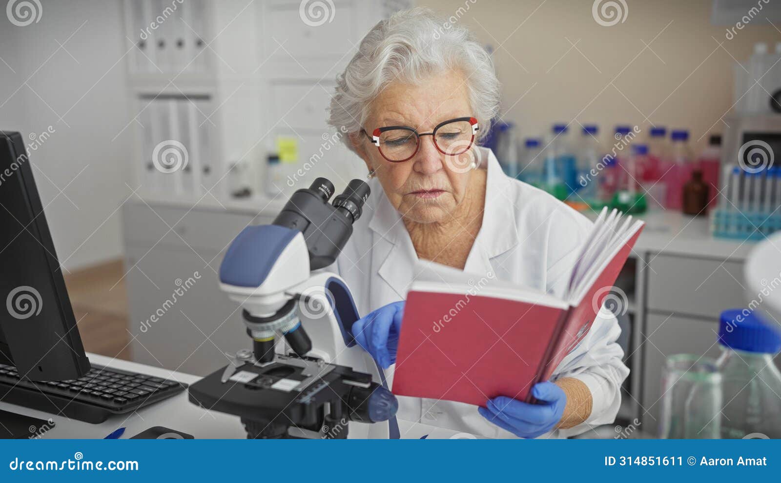 Senior Woman Scientist Reading a Book while Working with a Microscope ...