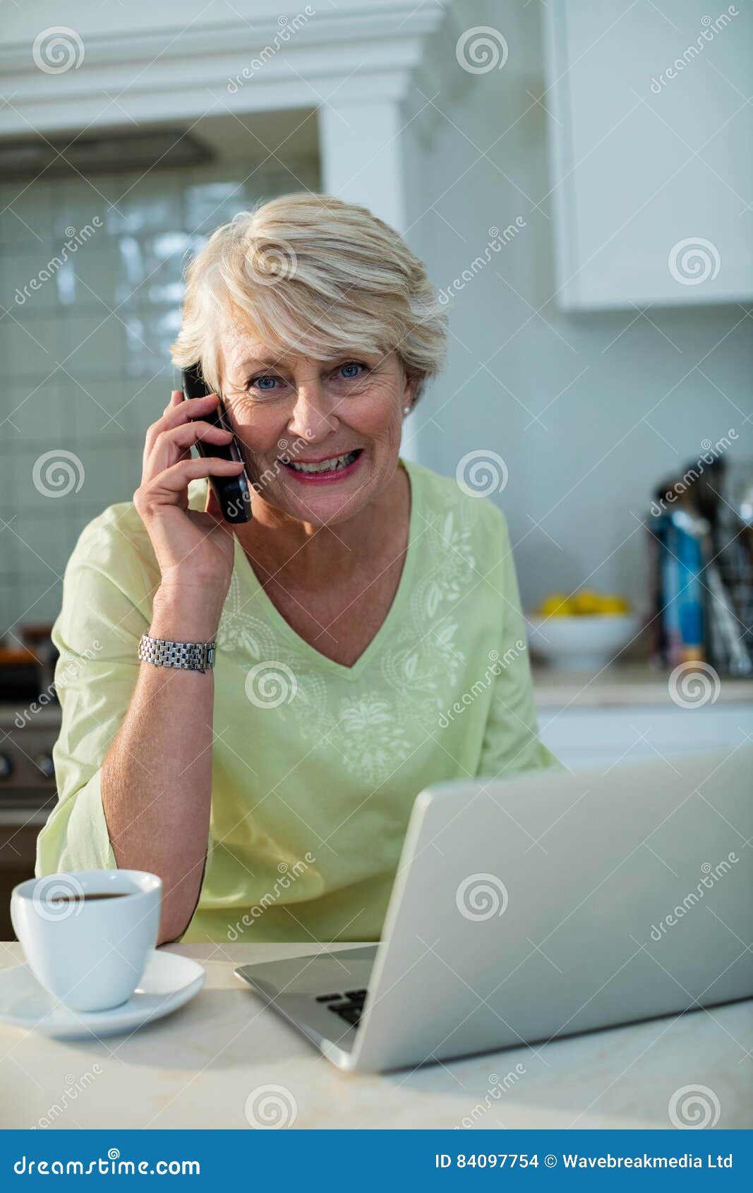 Senior Woman Sitting With Laptop And Talking On Mobile Phone Stock